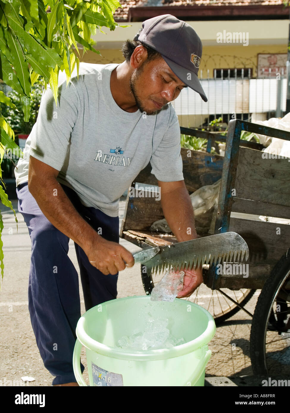 Local man cutting large chunks of ice from a block using serrated knife ...