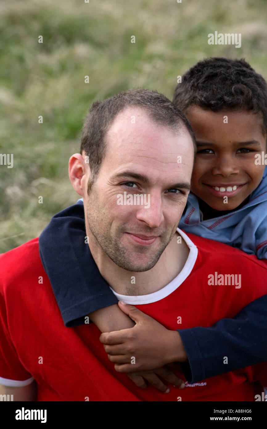Vertical portrait of young afro caribbean boy hugging his dad outdoors ...