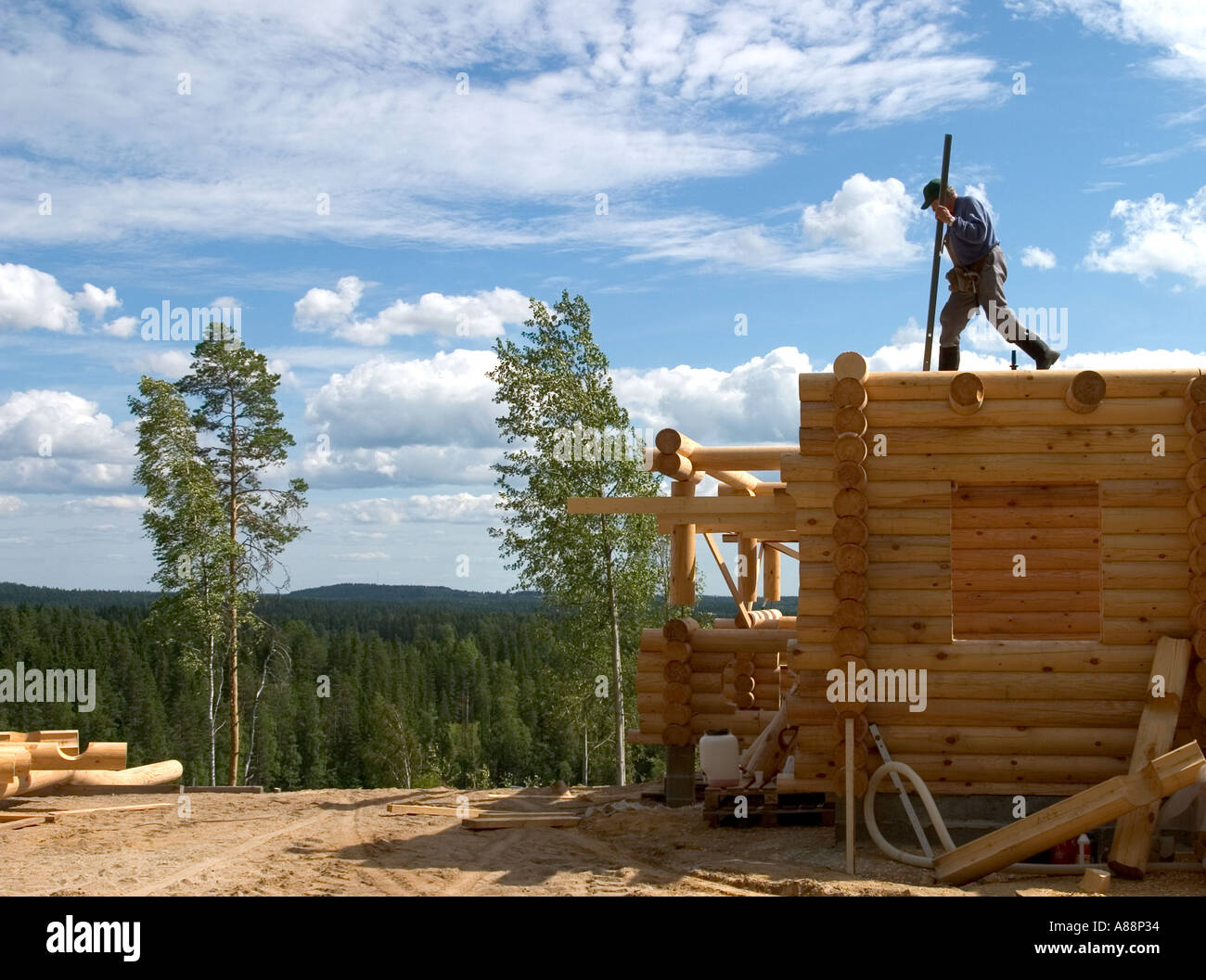 Elderly man building a log cabin and standing at the top of the cabin ...