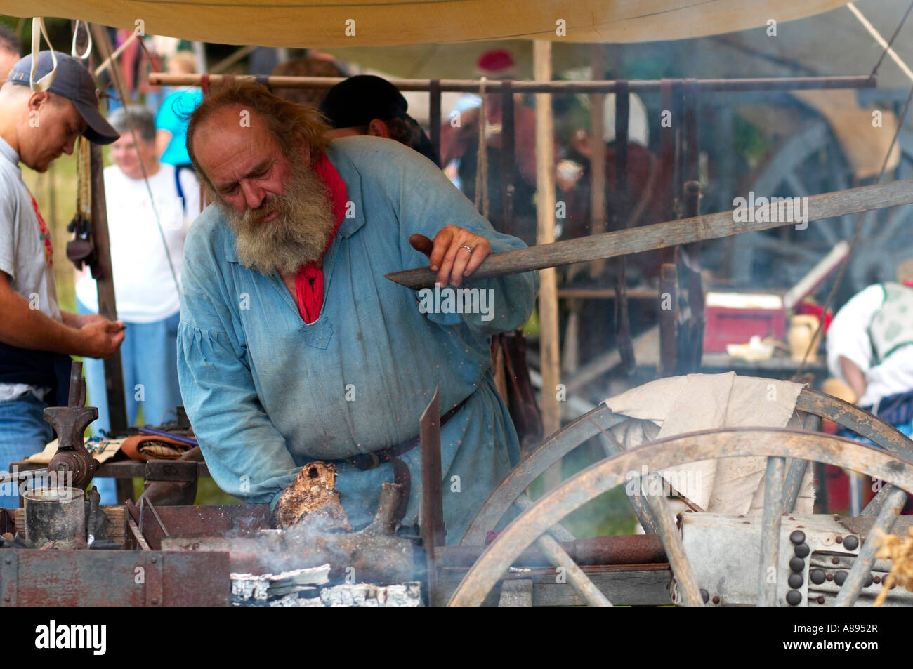 A man dressed in pre revolutionary clothing and hats using a blacksmith ...