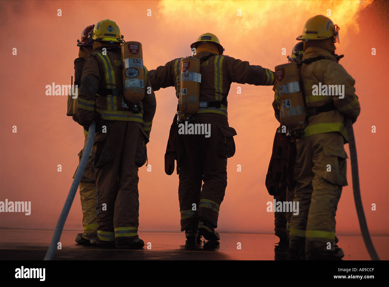 Three firefighters standing in an attack line using a fog sprayer ...