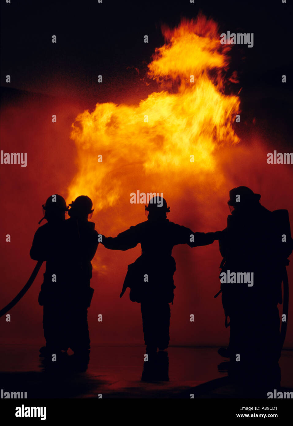 Three firefighters standing in an attack line using a fog sprayer ...