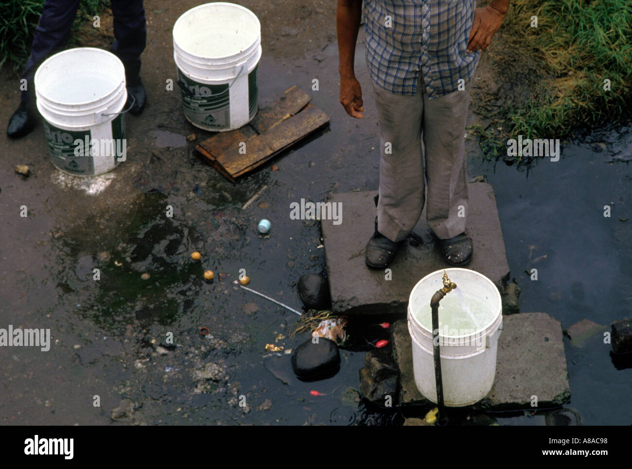 A man collects drinking water from public tap in the midst of a pool of ...