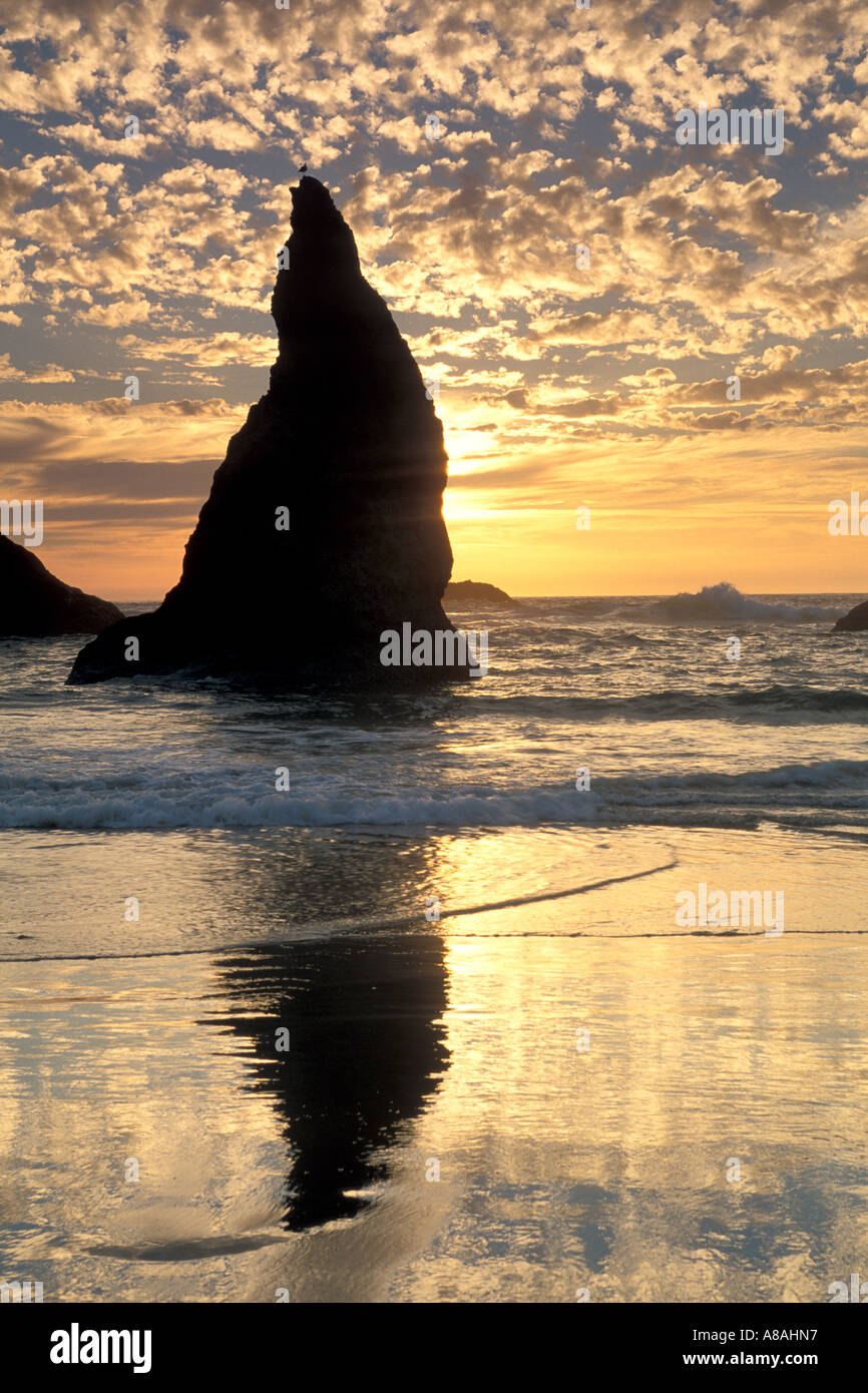 Clouds at sunset over jagged coastal rocks reflection in ocean waves ...