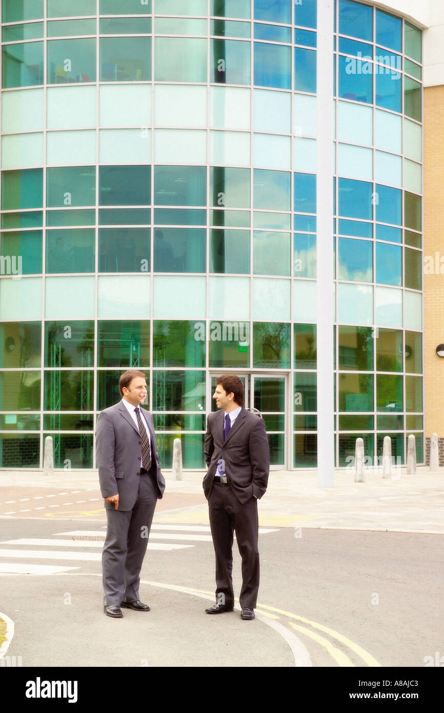Two Caucasian businessmen in suits standing outside a modern office ...
