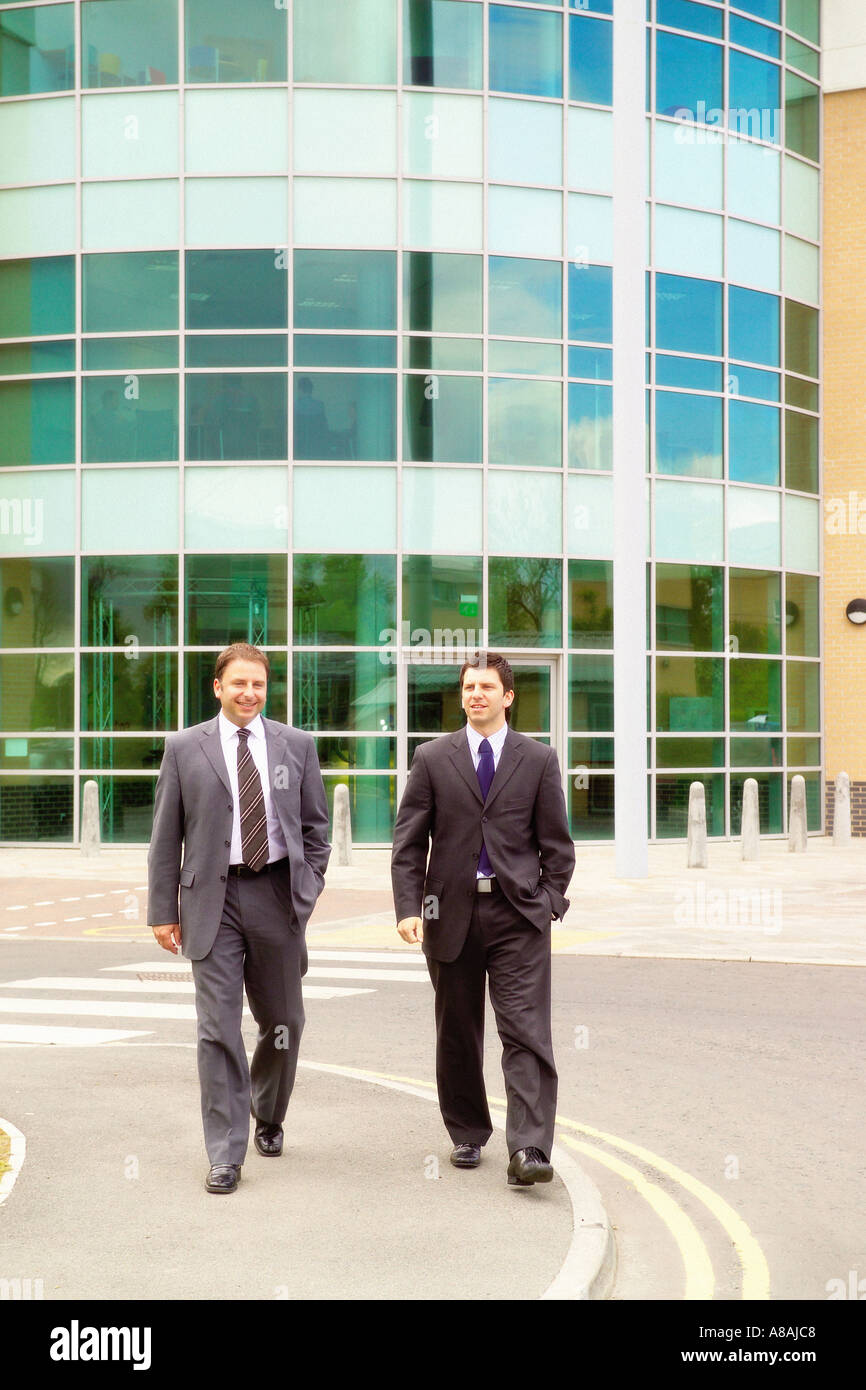 Two Caucasian businessmen in suits walk towards the camera outside a ...