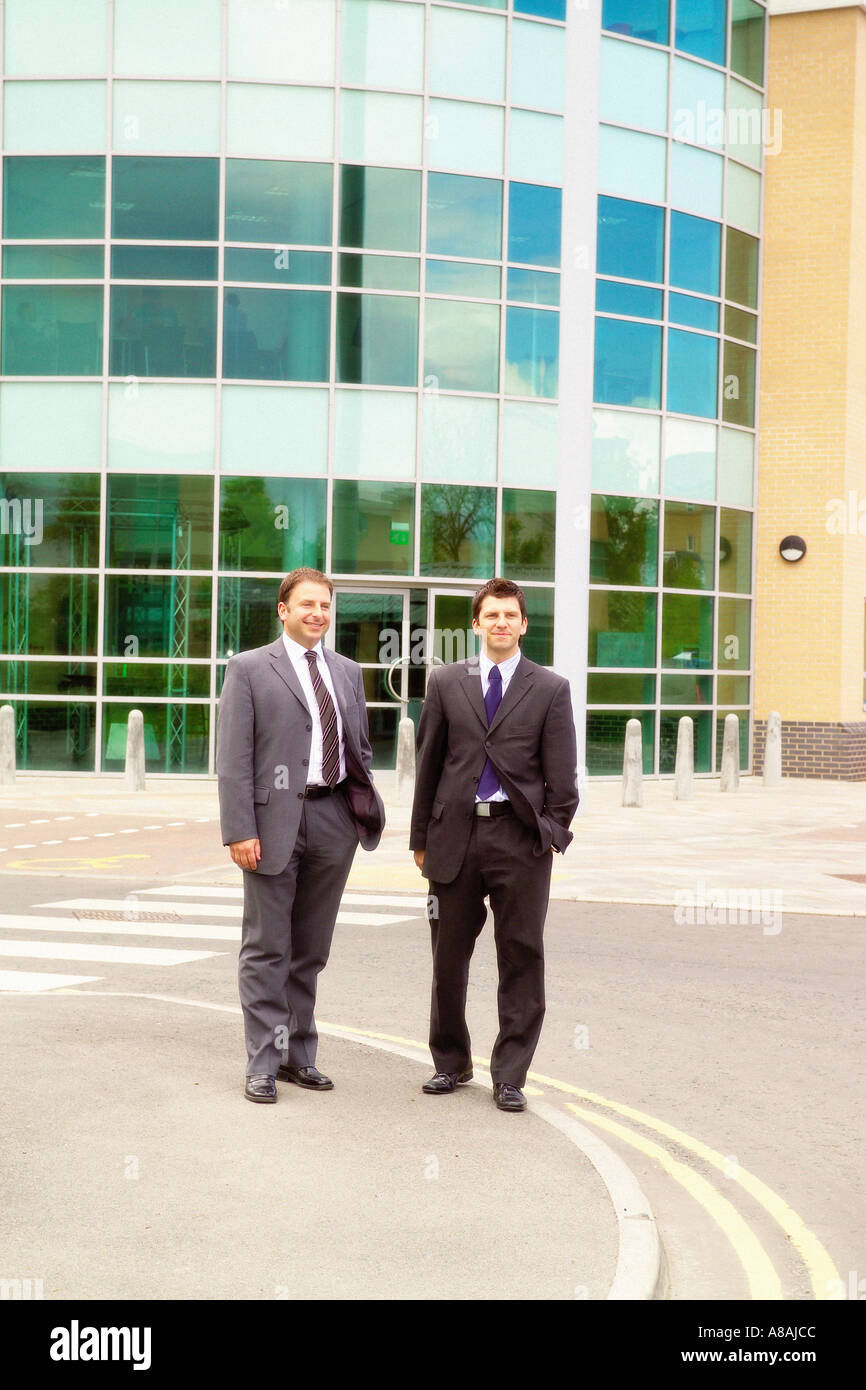 Two Caucasian businessmen in suits standing outside a modern office ...