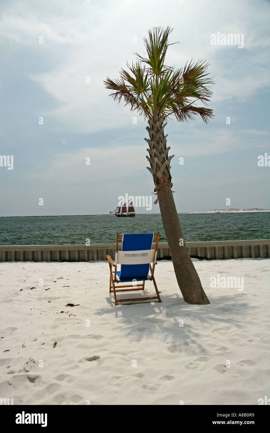Beach chair on sandy shore under shade of palm tree with sailboat in ...