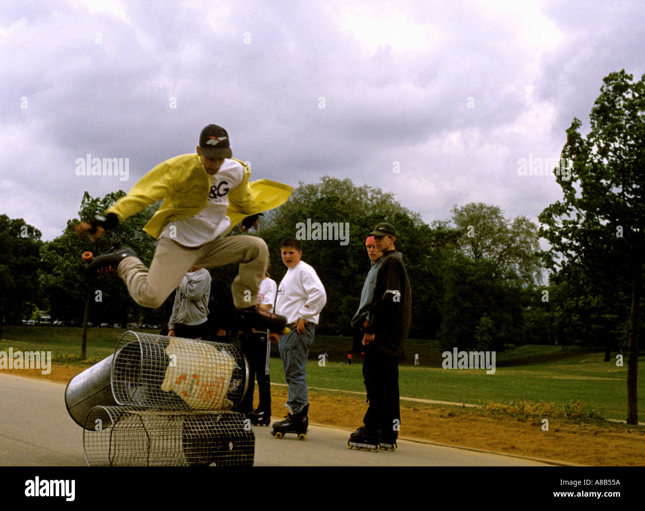 Youth jumping over rubbish bins in Hyde Park whilst friends look on ...
