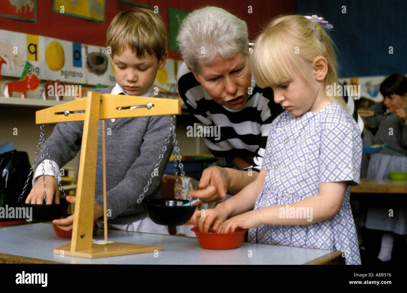 Teacher helping children at London preparatory school to weigh objects ...