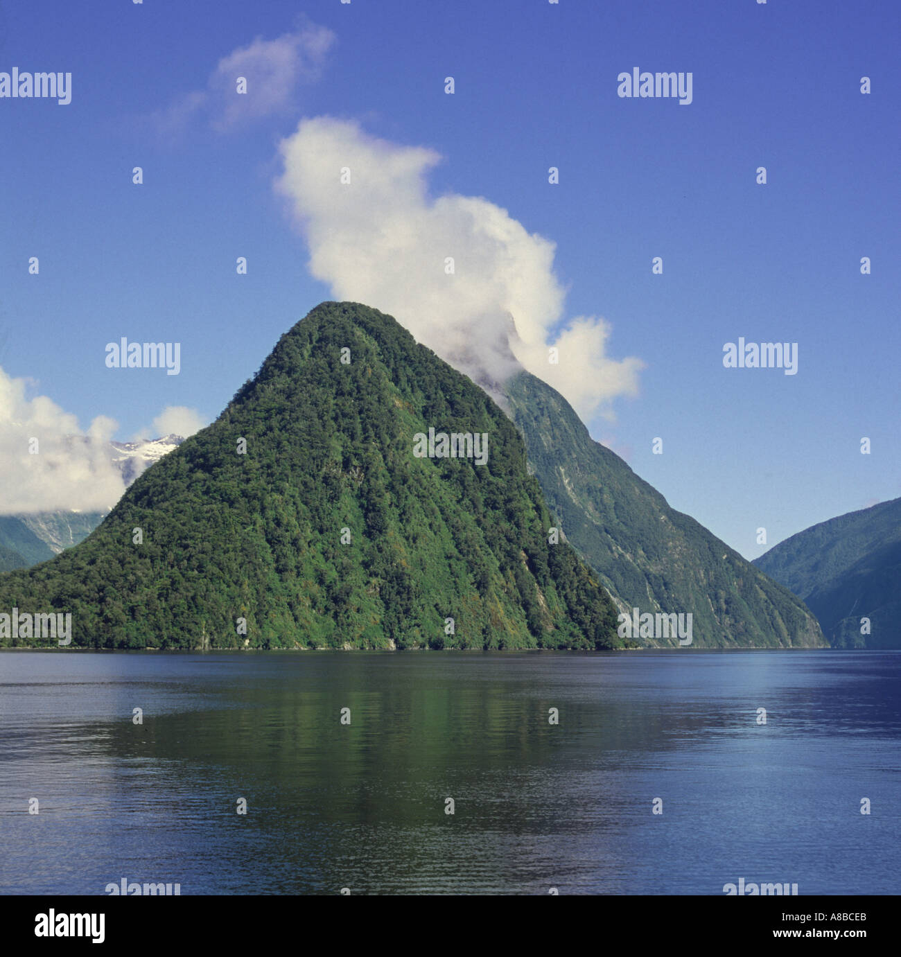 The steep pointed hill of Mitre Peak with white clouds over the top in ...