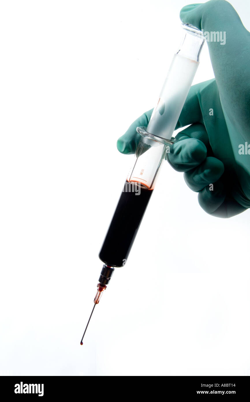 Hand in surgical glove holding large syringe with needle and droplet of ...