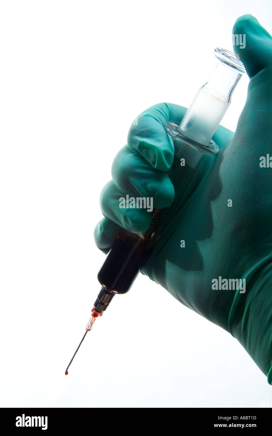 Hand in surgical glove holding large syringe with needle and droplet of ...