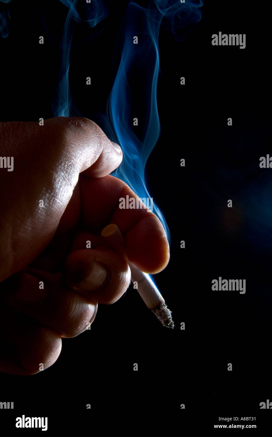 Hand holding smoking cigarette against black background Stock Photo - Alamy