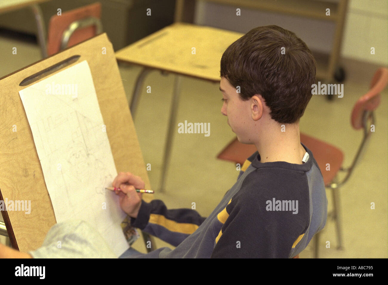 Student age 12 drawing at an easel in school art classroom. Golden ...
