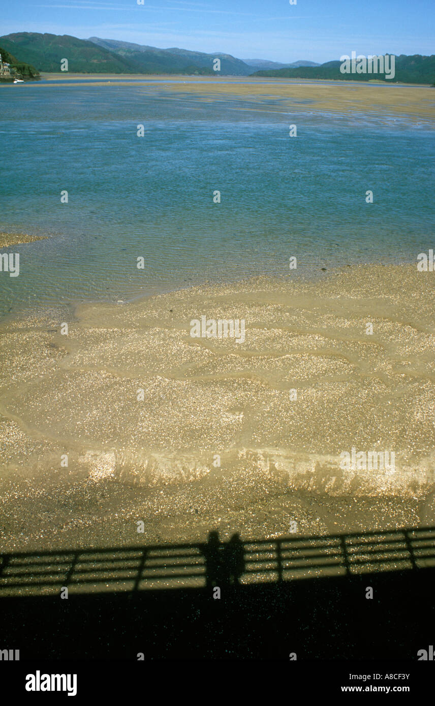 Shadow of two figures on railway footbridge looking over river estuary ...