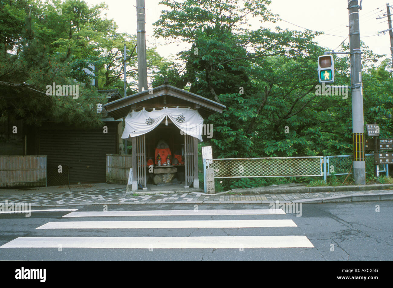 A pedestrian zebra crossing with a small Shinto shrine on the pavement ...