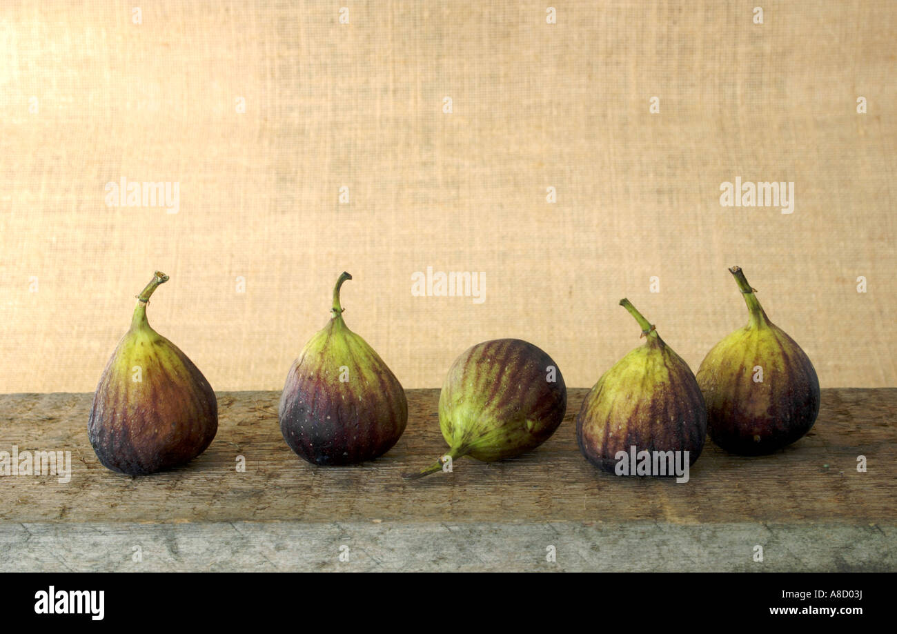 A still life of five ripe figs on a shelf against a Hessian background ...