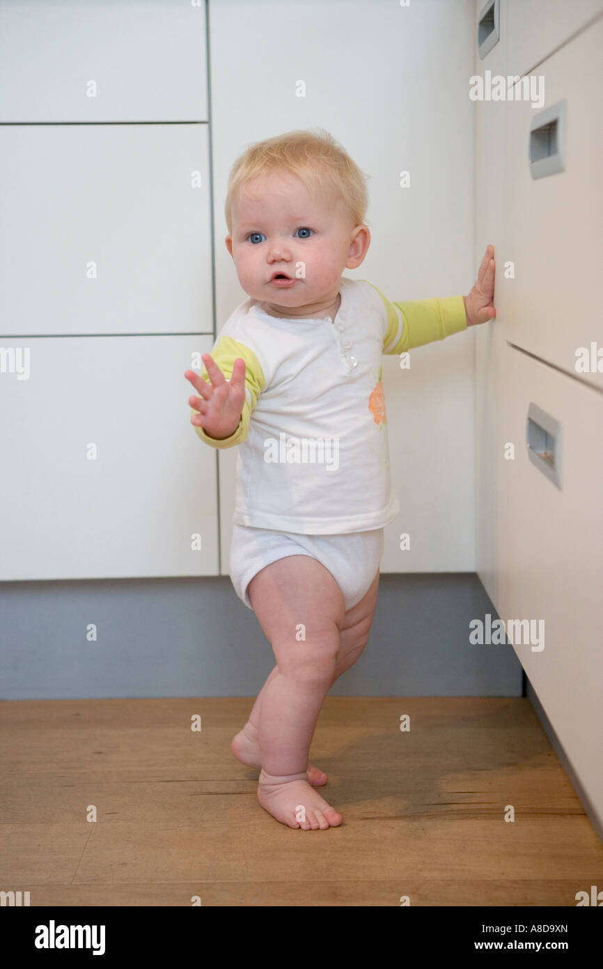 Baby standing against kitchen cupboard Stock Photo - Alamy