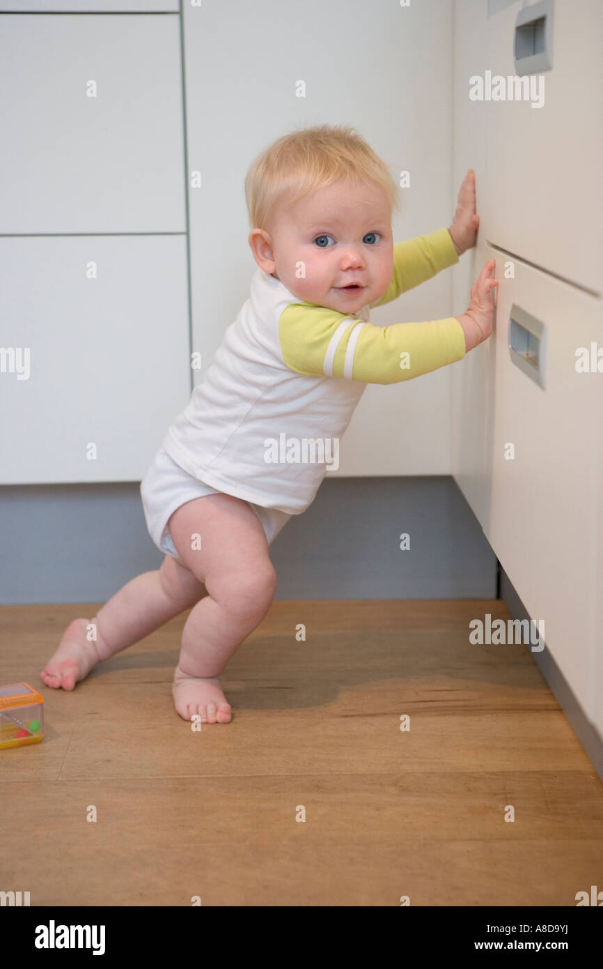Baby standing against kitchen cupboard Stock Photo - Alamy