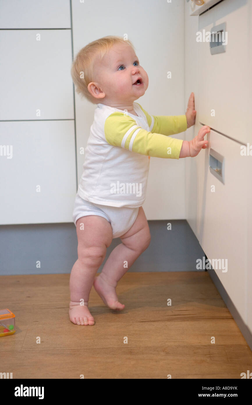 Baby standing against kitchen cupboard Stock Photo - Alamy
