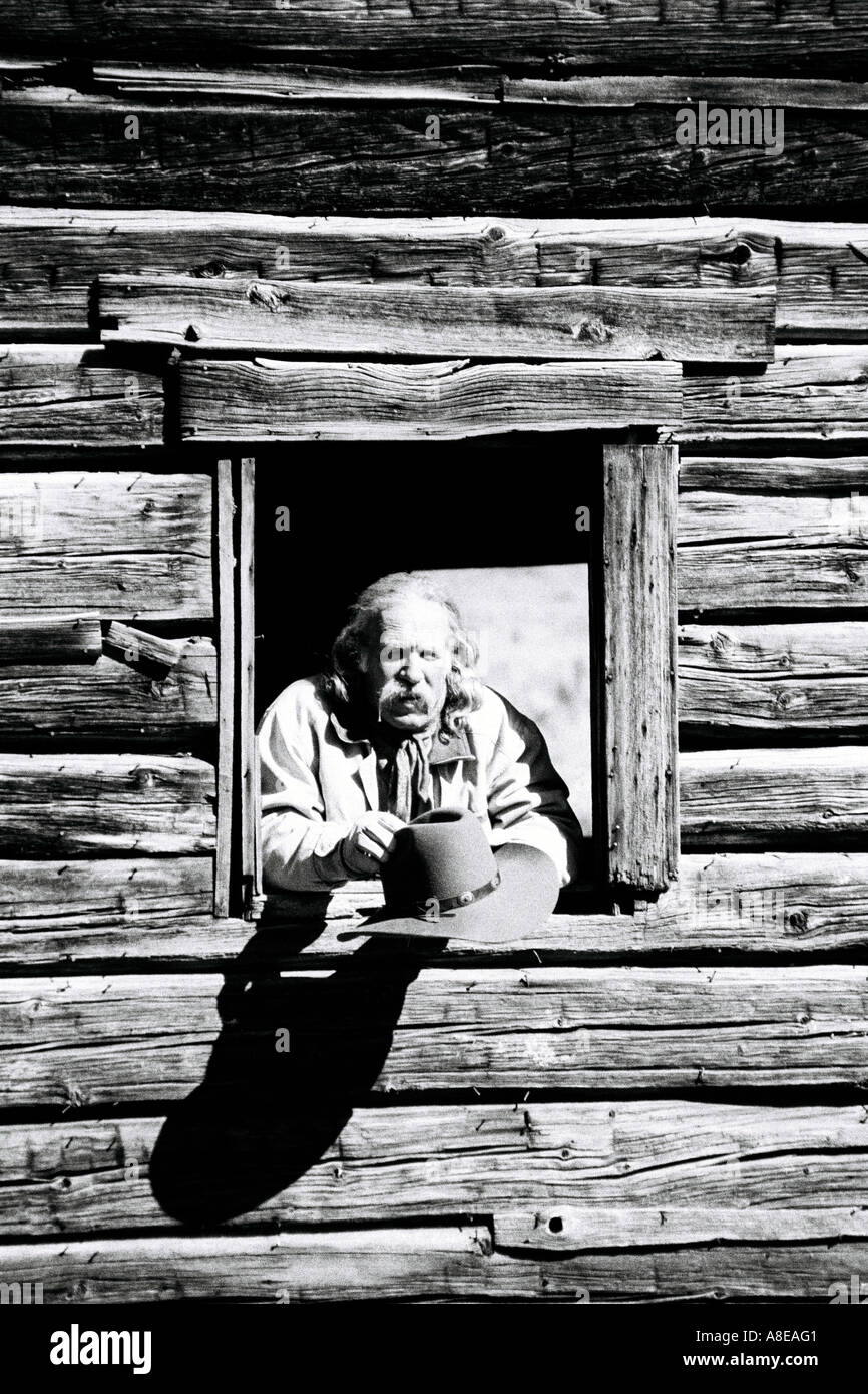 A cowboy in the window of a rustic cabin with his hat off Stock Photo ...