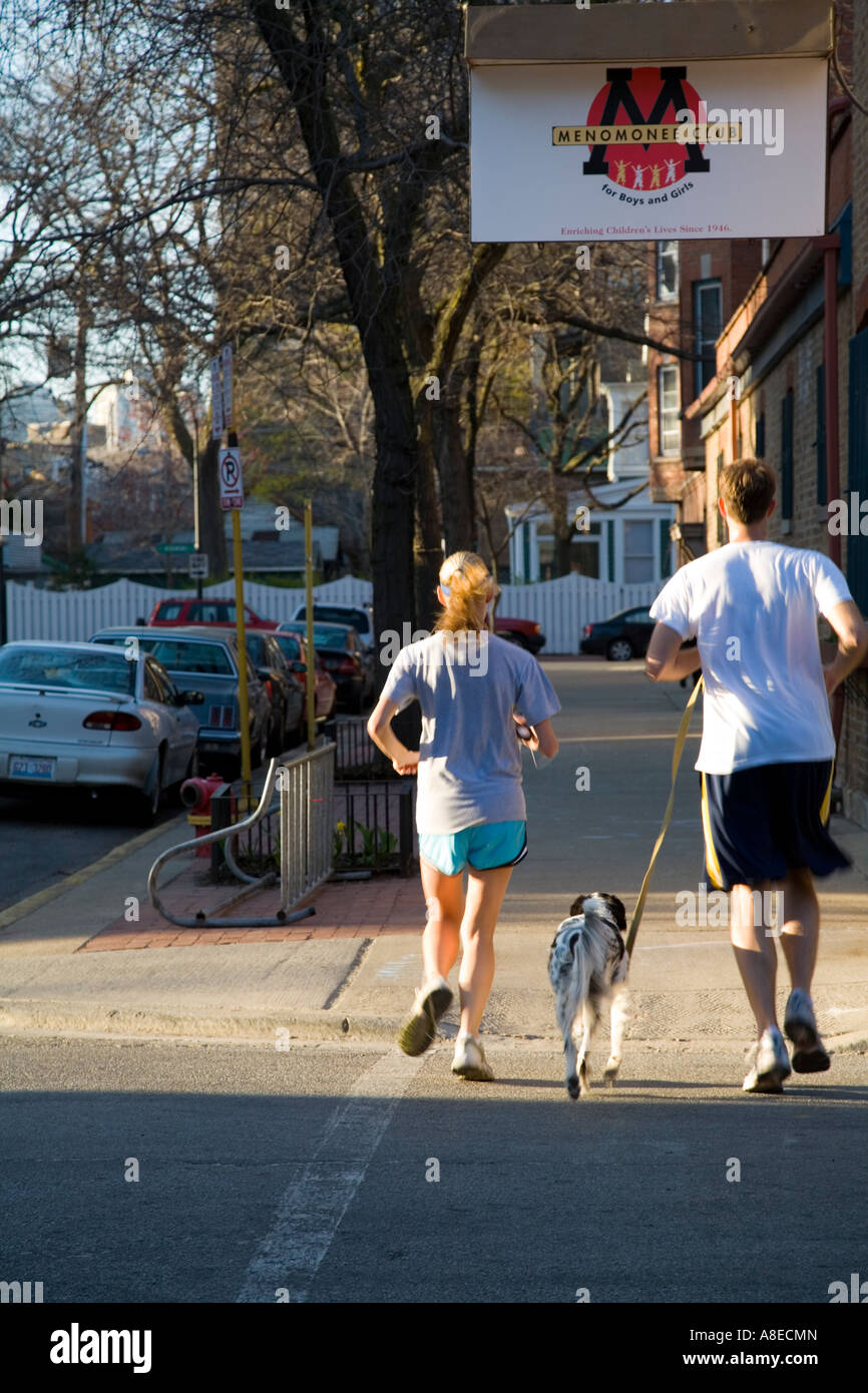 CHICAGO Illinois Young adult couple run with leashed dog on sidewalk in ...