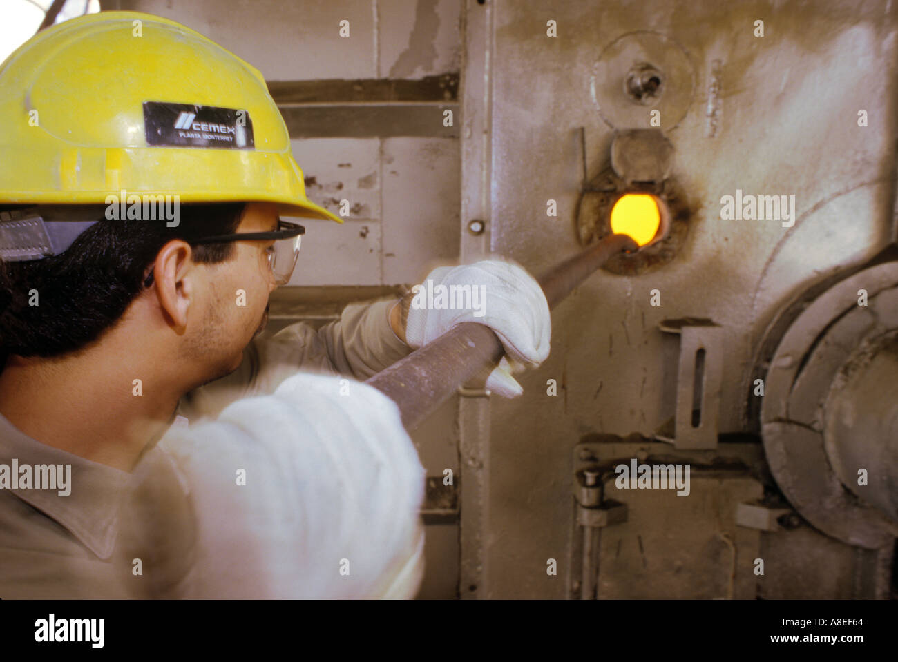 A worker samples the contents of a furnace at the Cemex cement plant in ...
