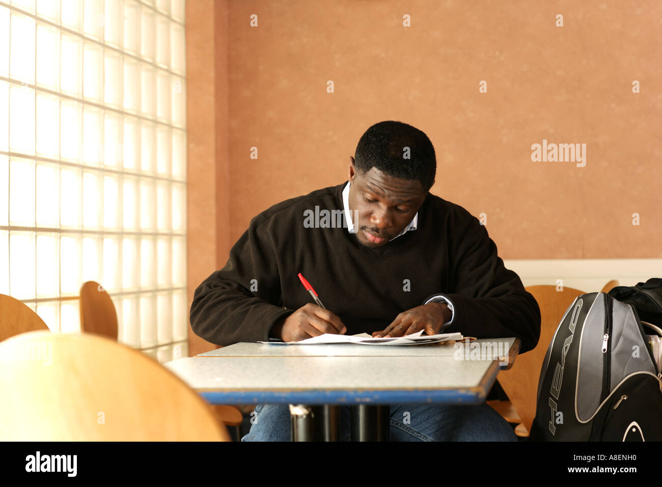 Black student studying in an open area at University, he is writing at ...
