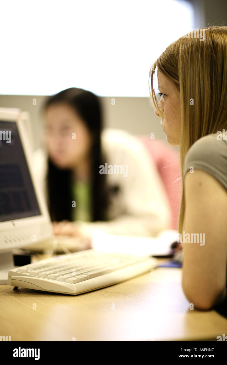 Young blonde feamle student is working at a computer, a chinese girl is ...