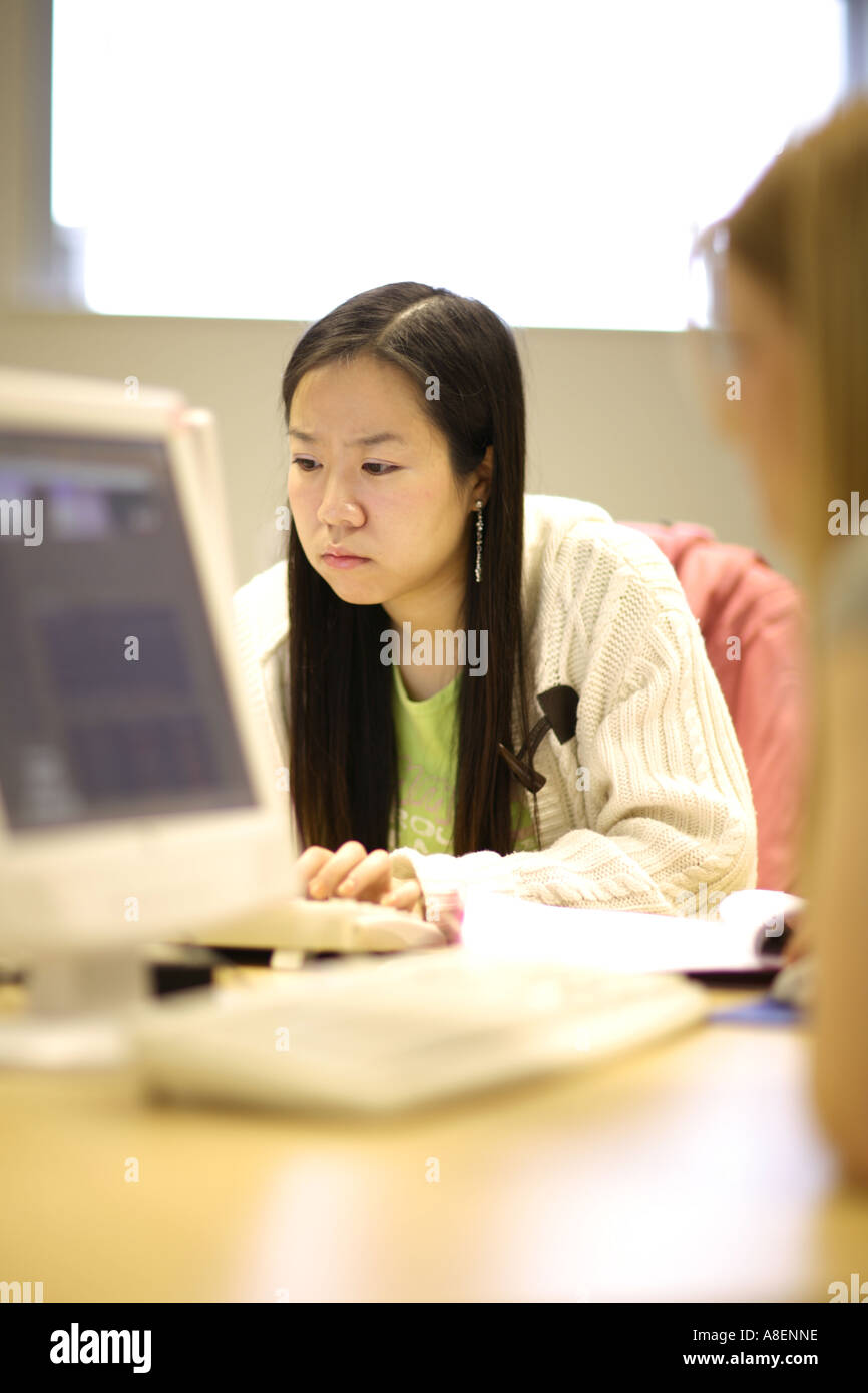 Young chinese female student works at a computer at univeristy, another ...