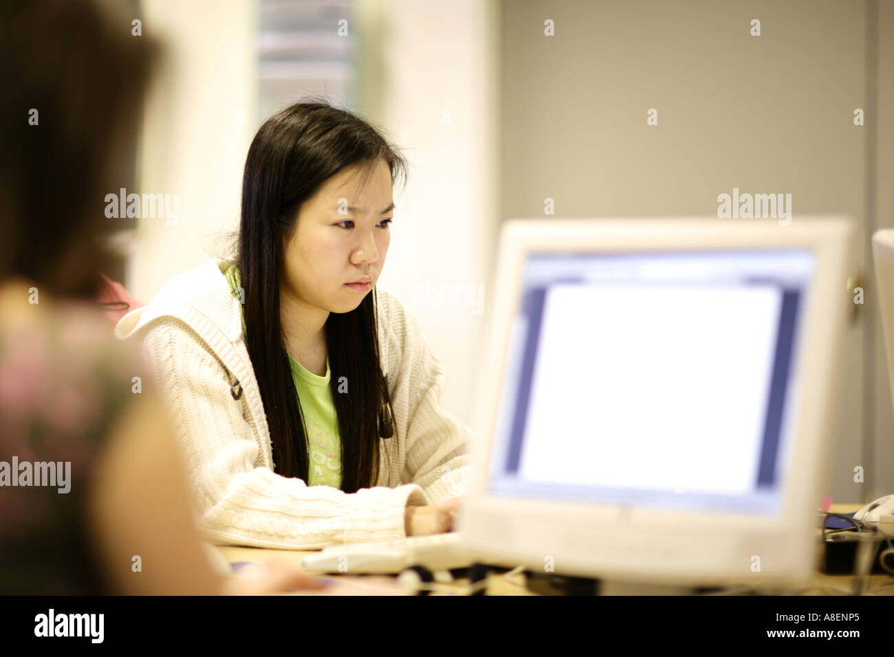 Young chinese female student works at a computer at univeristy, another ...