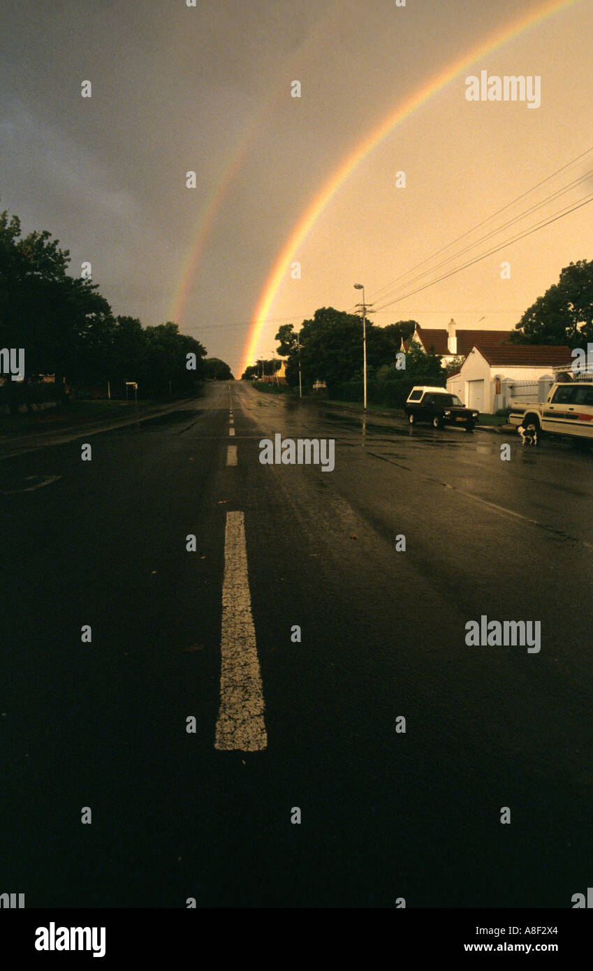 A colourful rainbow starts in the middle of a long straight road Stock ...