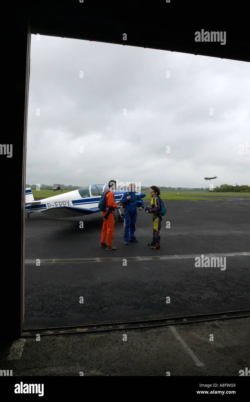Three persons wearing parachute gear waiting near small plane Stock ...