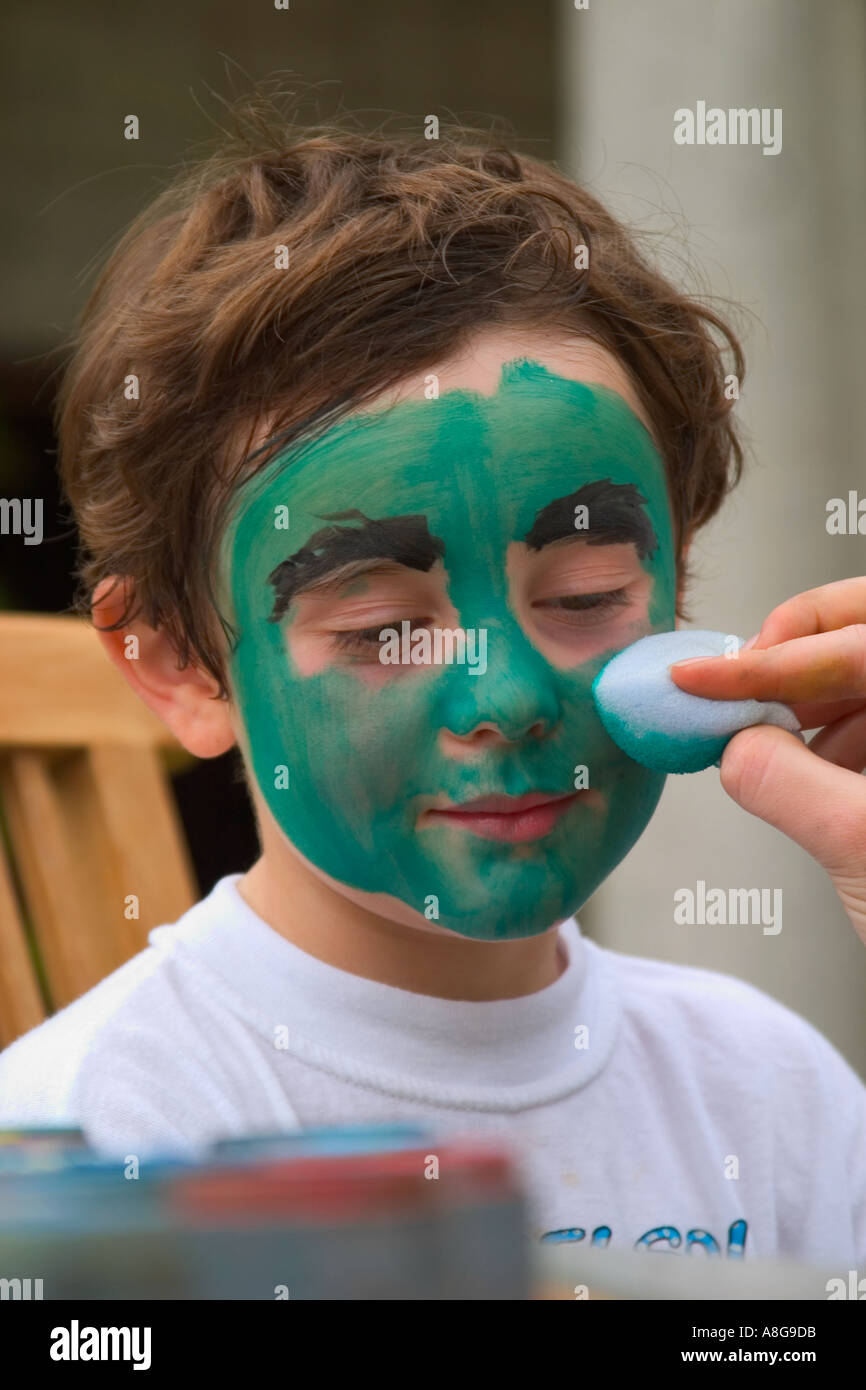 Portrait of child with subtle knowing smile being face painted green ...