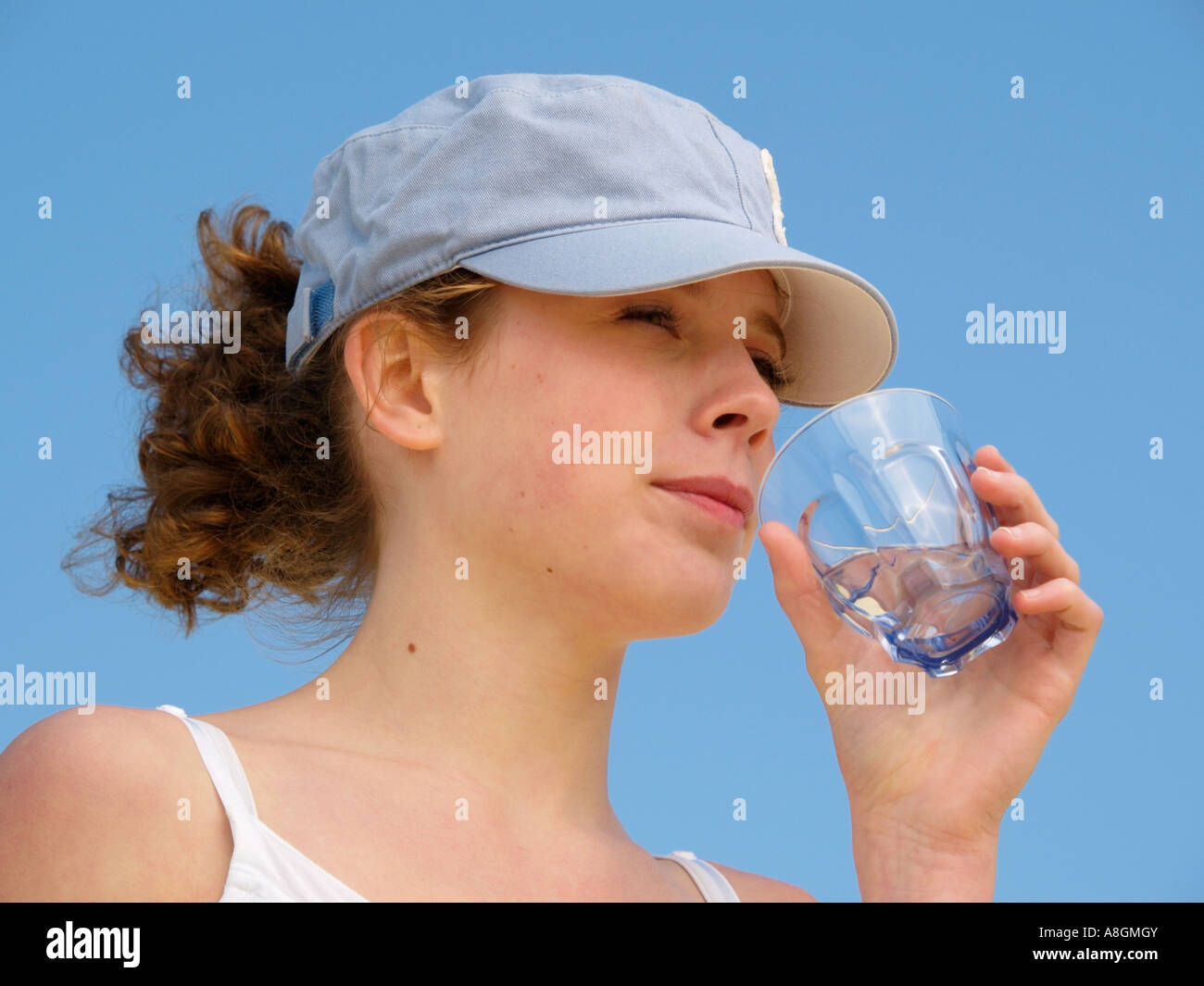 Young woman wearing light blue cap drinking glass of water against blue ...