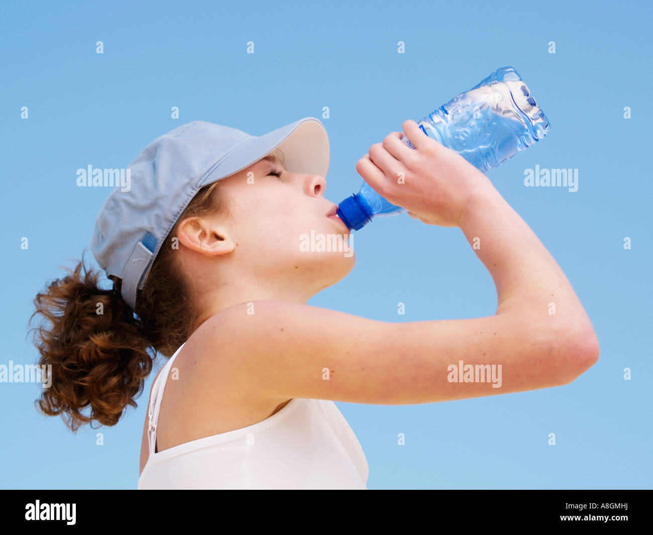 Teenage girl wearing light blue cap drinking bottled water against blue ...