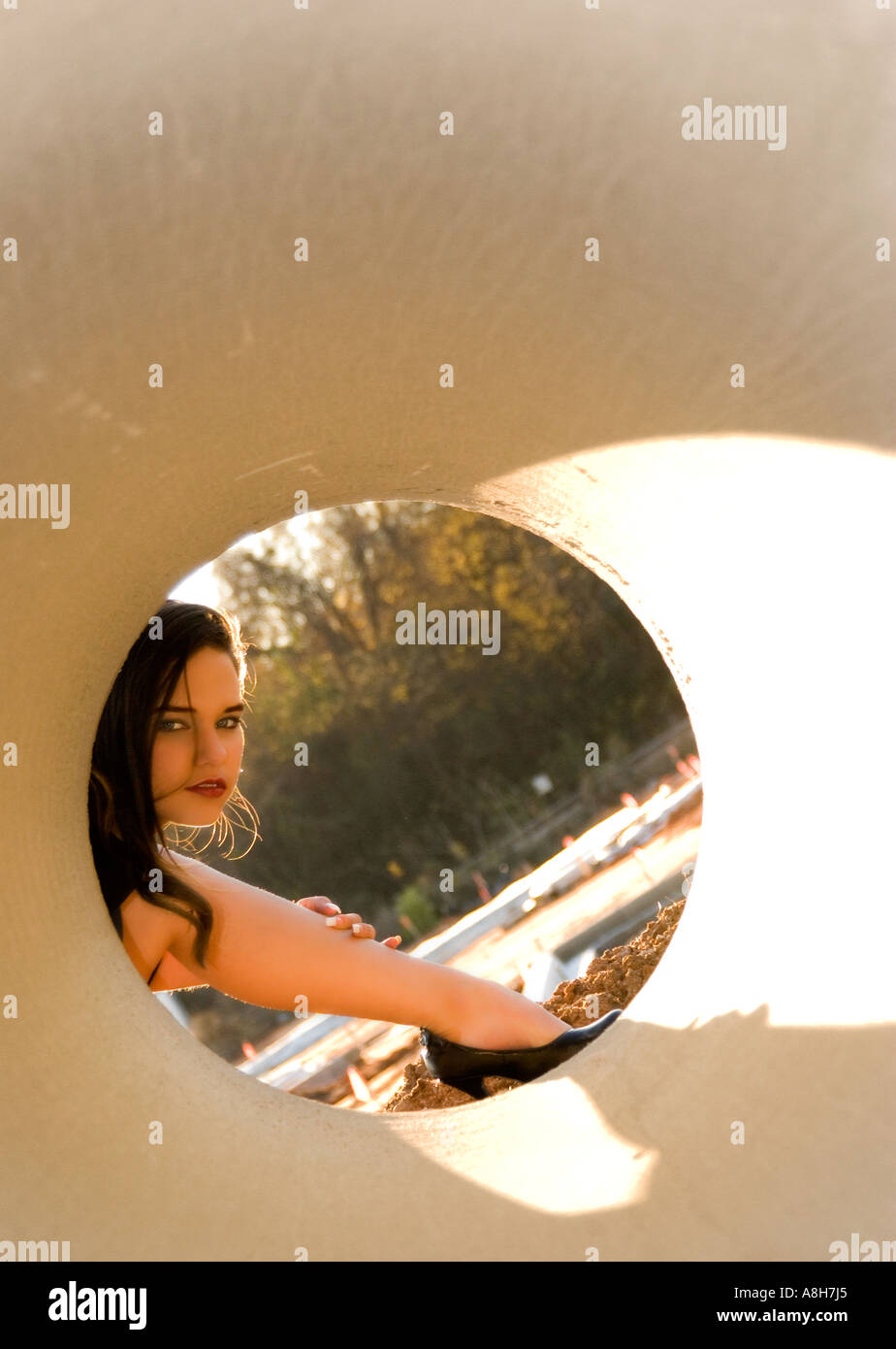 Beautiful Caucasian teen girl (18-19) peers through a large drainage ...