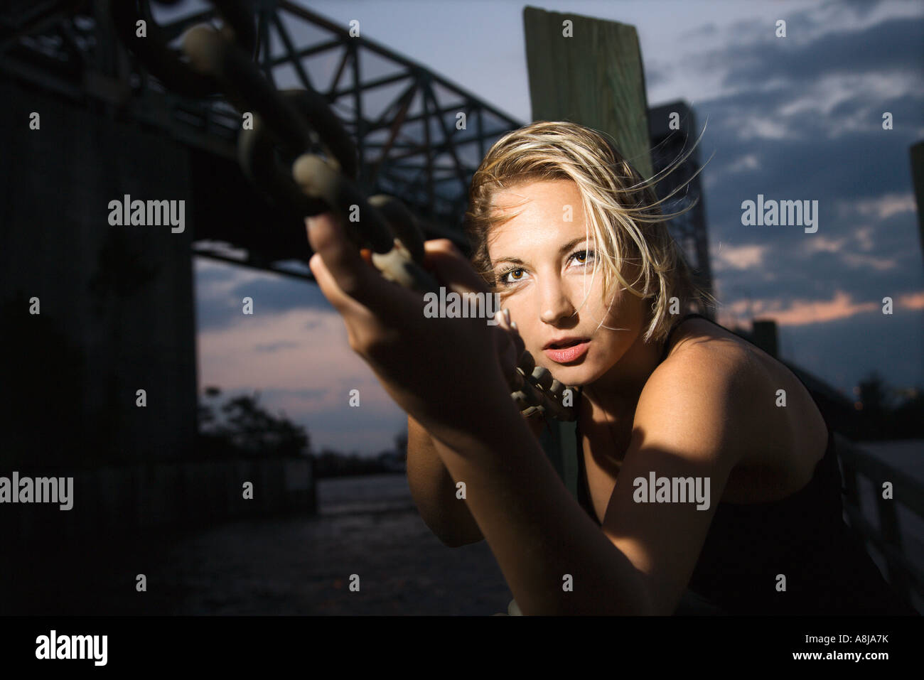 Caucasian mid adult blonde woman clinging to chain rail beside bridge ...