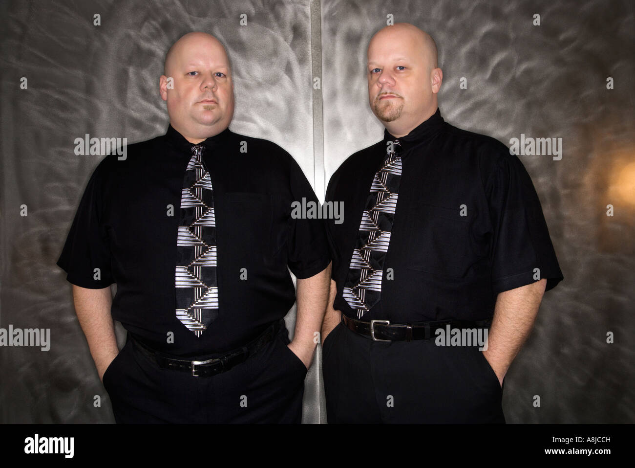 Caucasian bald mid adult identical twin standing together looking at ...