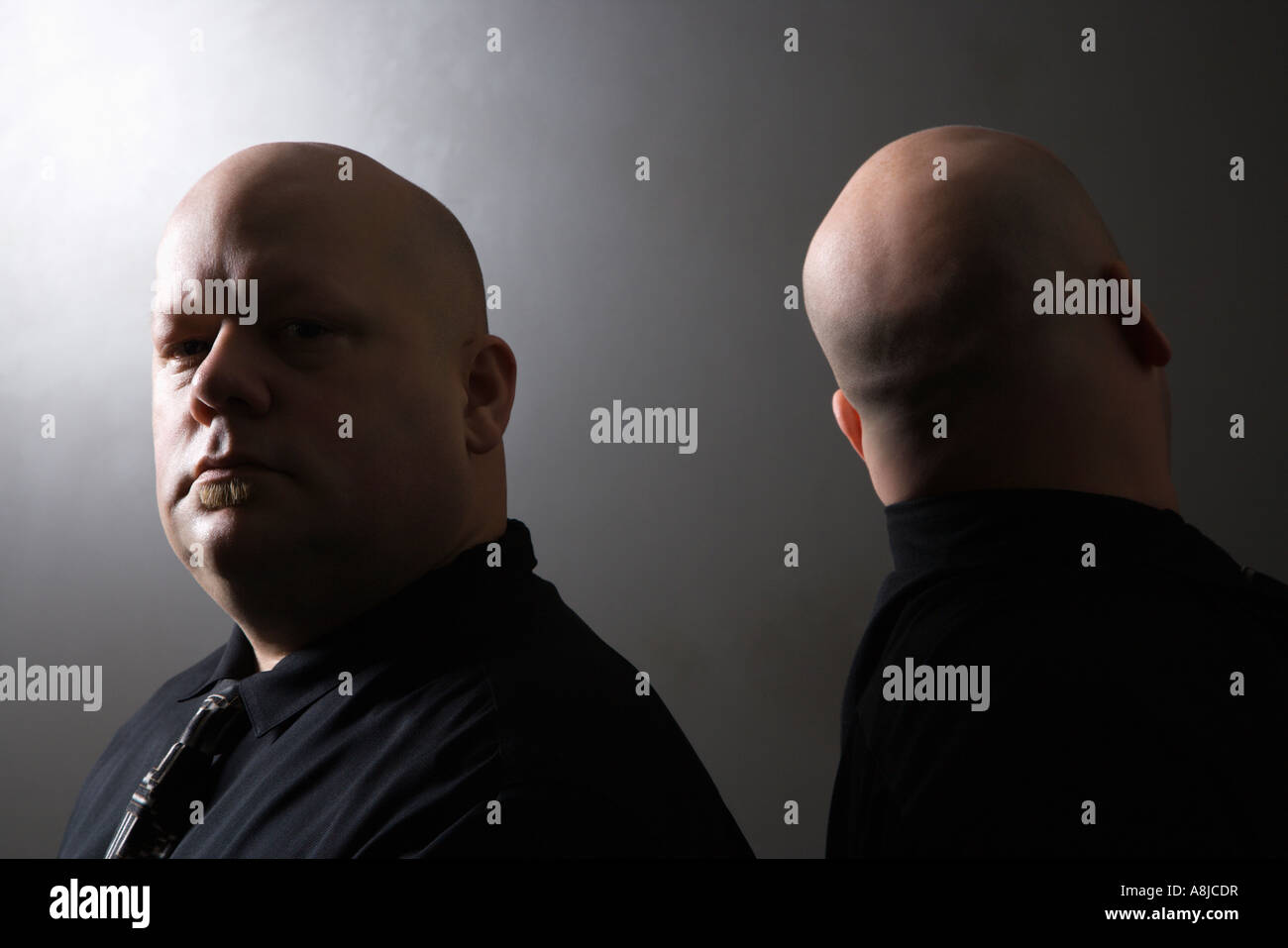 Caucasian mid adult bald identical twin men standing back to back and ...