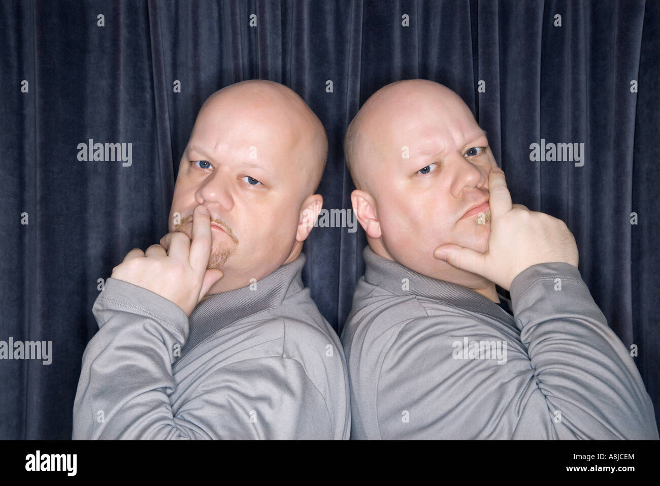 Caucasian bald identical twin men standing back to back and looking at ...