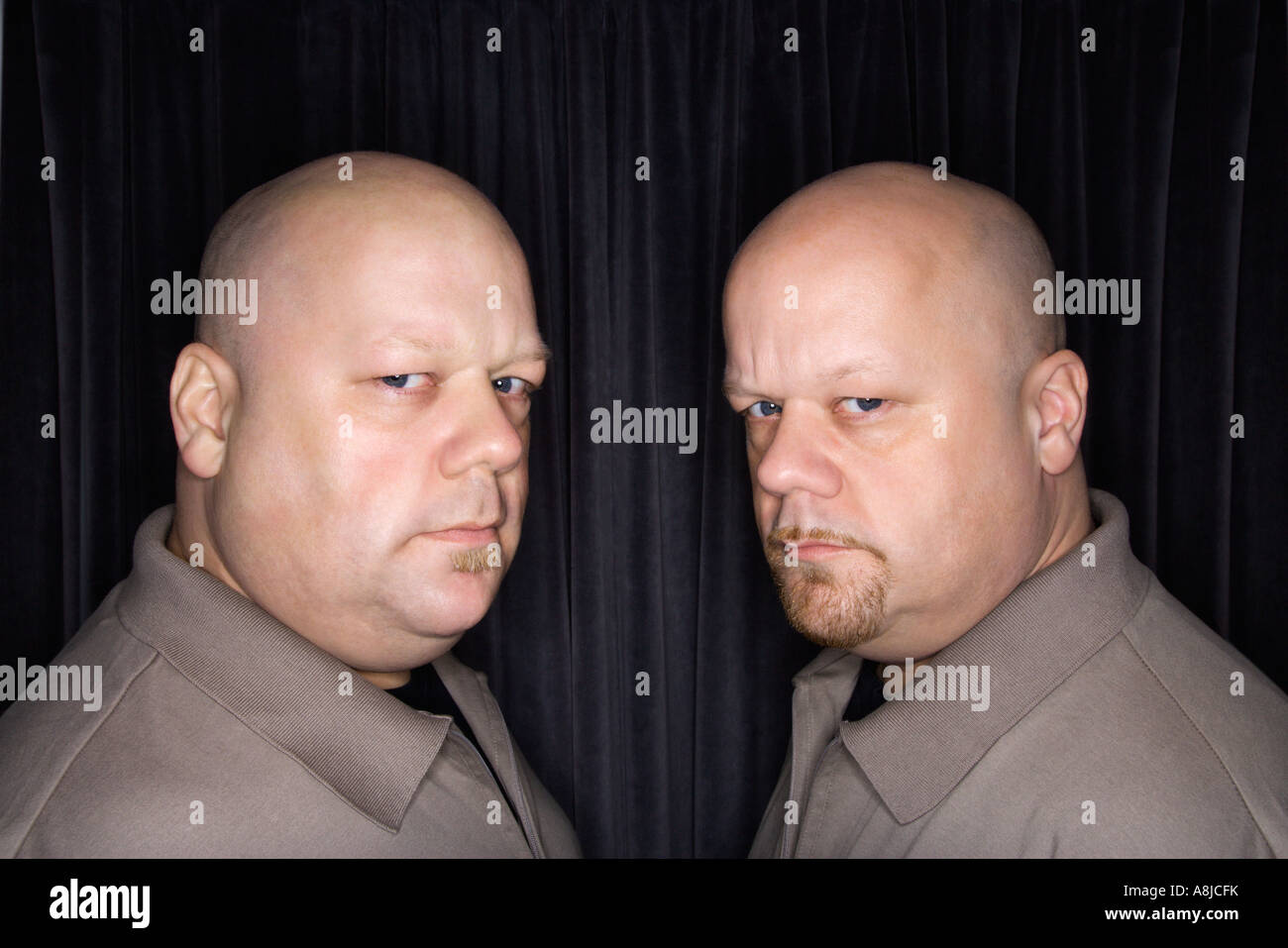 Caucasian bald mid adult identical twin men looking sternly at viewer ...