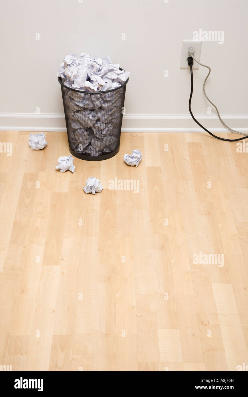 Full wire mesh trash can with crumpled paper next to electrical outlet ...