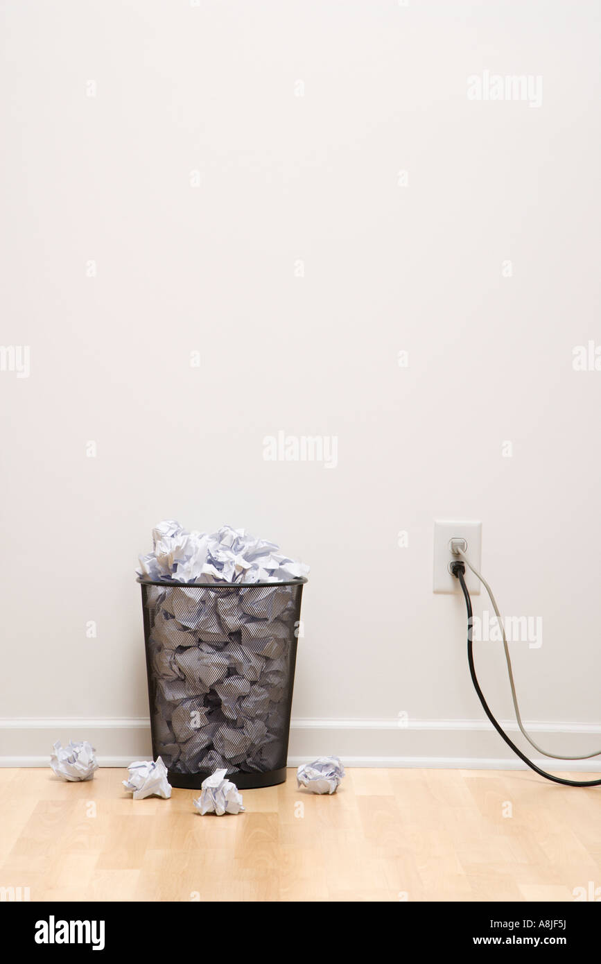 Full wire mesh trash can with crumpled paper next to electrical outlet ...