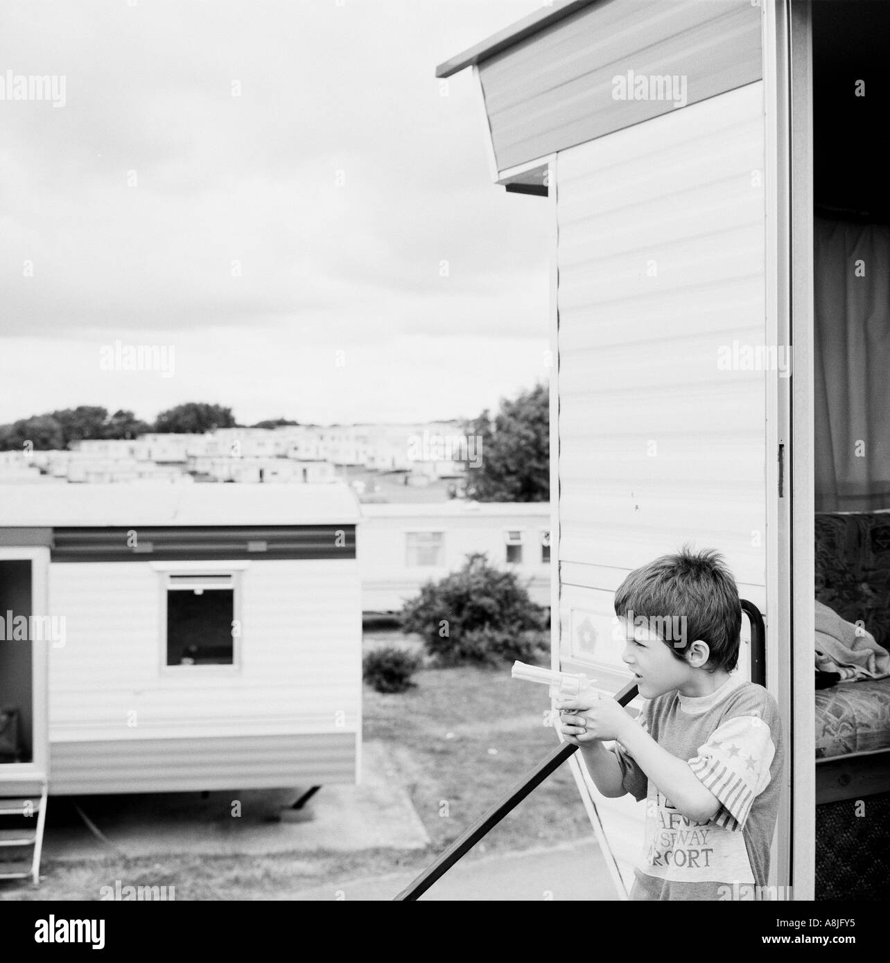 A boy plays with a water pistol on the steps of a caravan in a holiday ...
