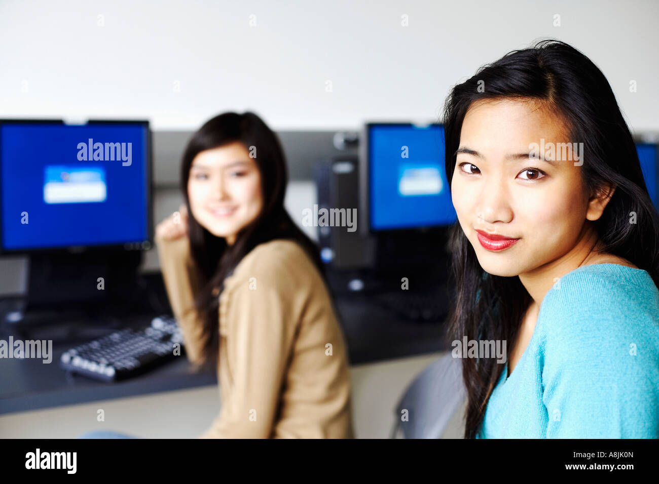 Portrait of two young women sitting in front of computers and smiling ...
