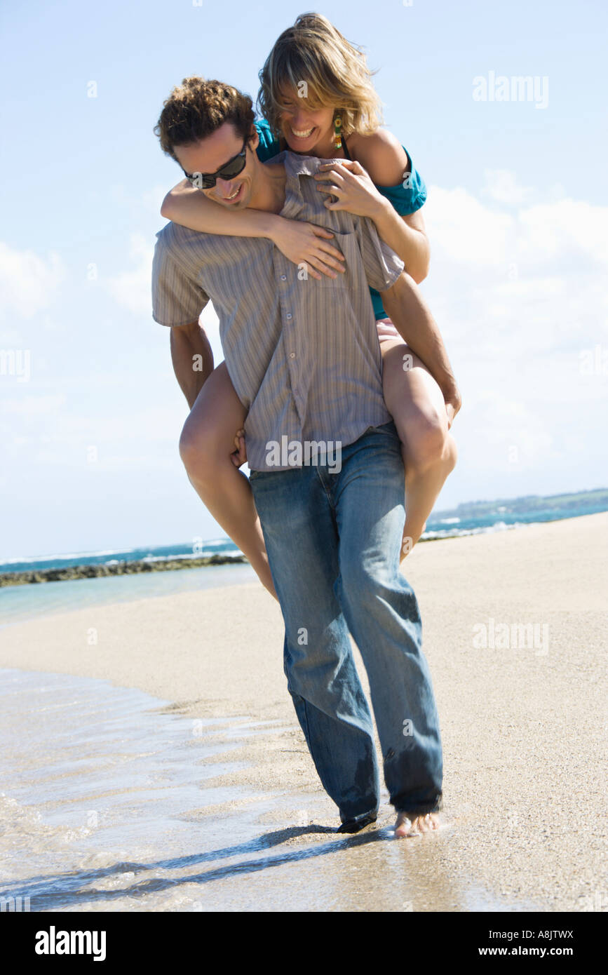 Mid adult Caucasian man giving woman piggyback ride on beach Stock ...