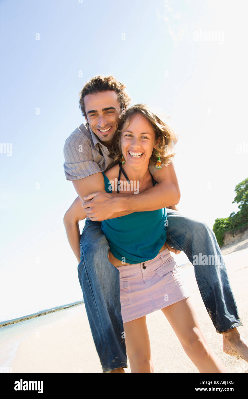 Mid adult Caucasian woman giving man piggyback ride on beach Stock ...