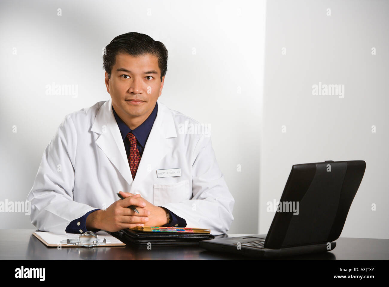 Asian American male doctor sitting at desk with charts and laptop ...